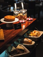 Exposição de sobremesas com bolo, potes e cestas de pão sobre um balcão de madeira.
