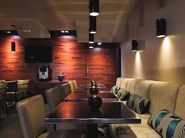 Uma sala de jantar moderna com uma mesa comprida, cadeiras e um sofá com almofadas estampadas.