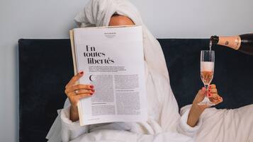 Uma pessoa lendo um livro na cama enquanto champanhe é servido em uma taça.