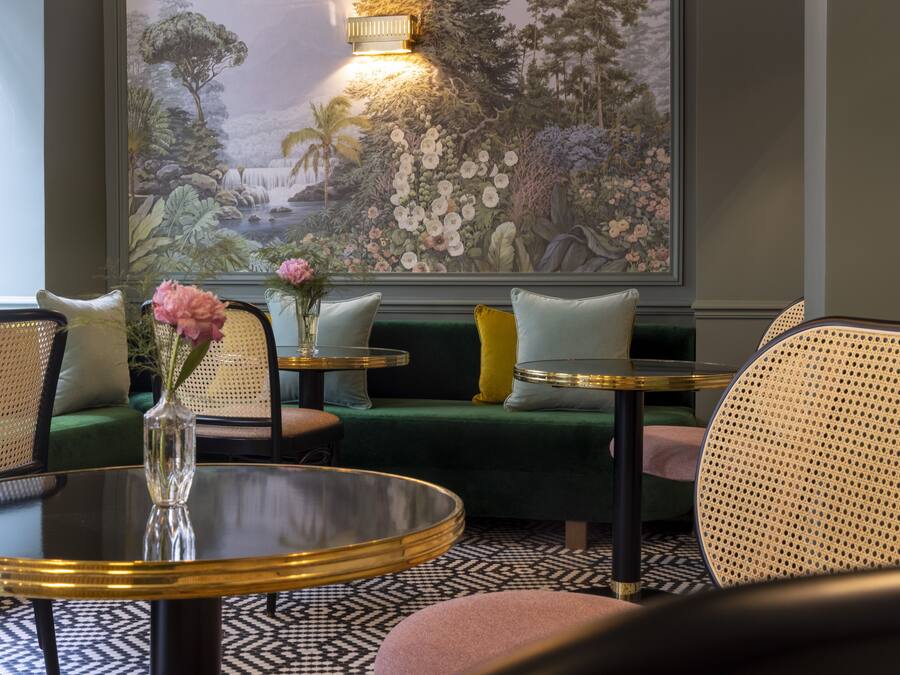 Quarto com sofá verde, mesa redonda com um vaso de flores e um mural de paisagem tropical.