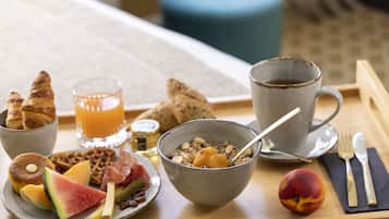 Bandeja de café da manhã com croissants, waffles, frutas, uma tigela de cereal, um copo de suco de laranja e uma xícara de café.