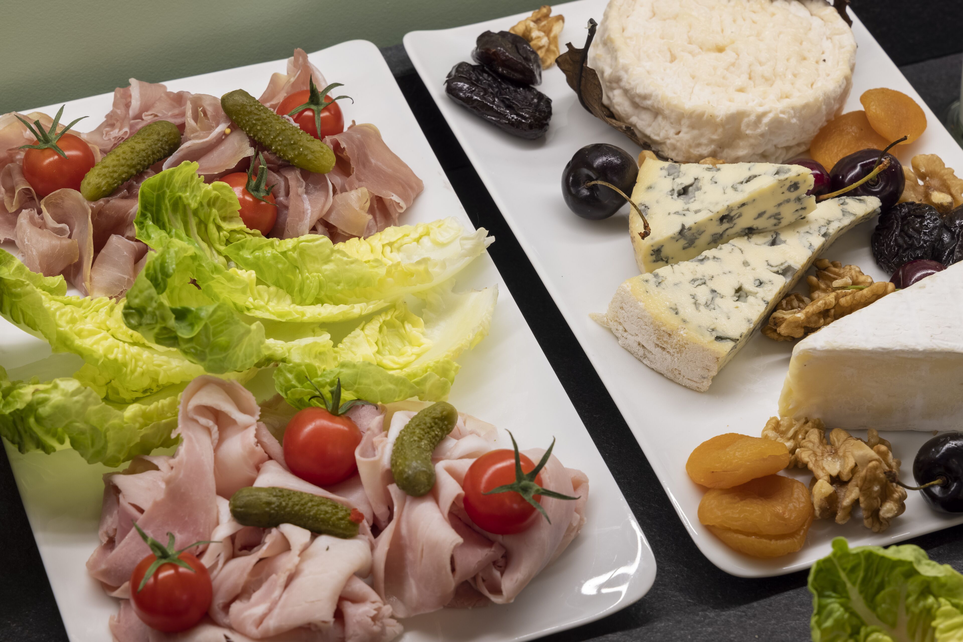 Uma travessa com diversos queijos, carnes e frutas.