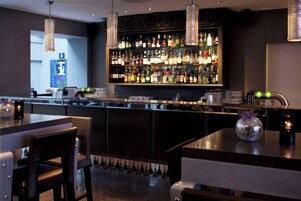 Uma área de bar com uma prateleira de bebidas bem abastecida, luminárias pendentes e um balcão moderno.