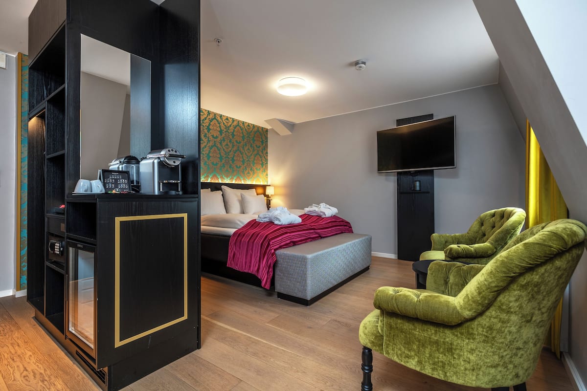 Quarto de hotel moderno com cama, poltrona verde, televisão de tela plana e minibar.
