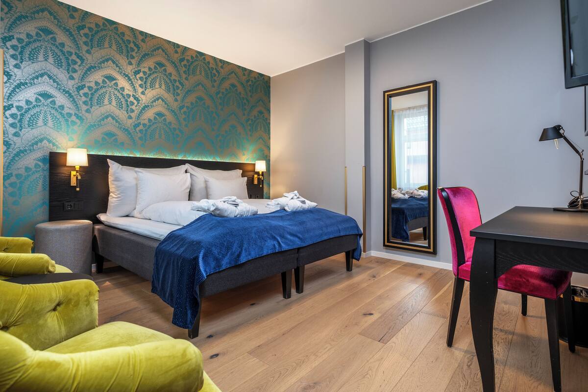 Quarto de hotel moderno com uma cama grande, uma escrivaninha, uma cadeira e um espelho.