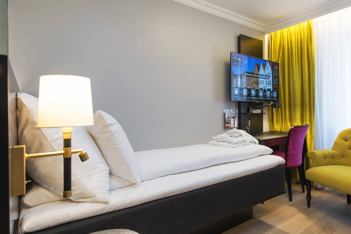 Quarto de hotel com uma cama, uma escrivaninha, uma televisão e uma cadeira.