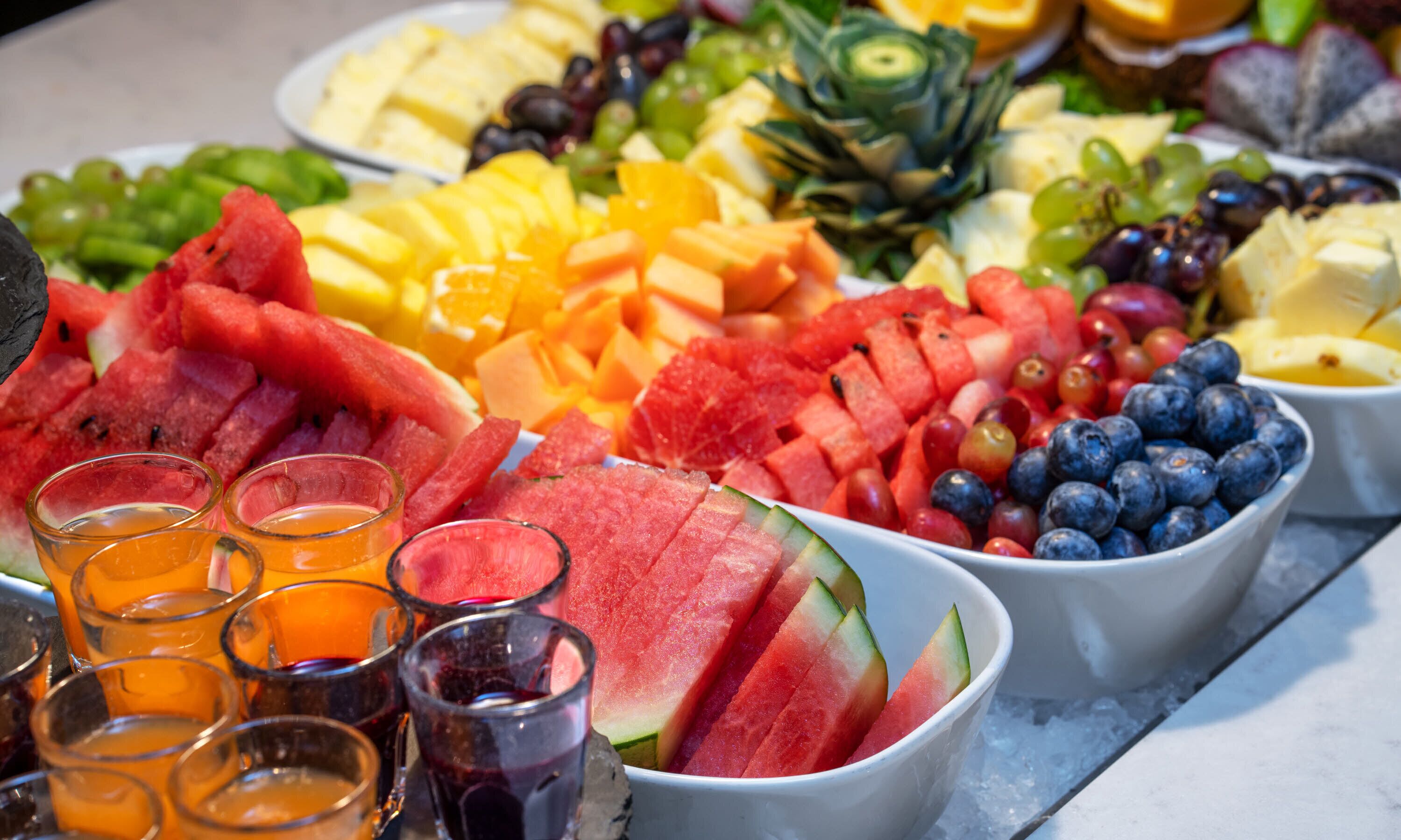 Uma tábua de frutas com diversos tipos de frutas e potes com bebidas.