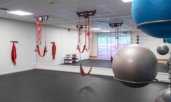 Uma academia com equipamentos para yoga aérea, bolas de exercício e um espelho grande.