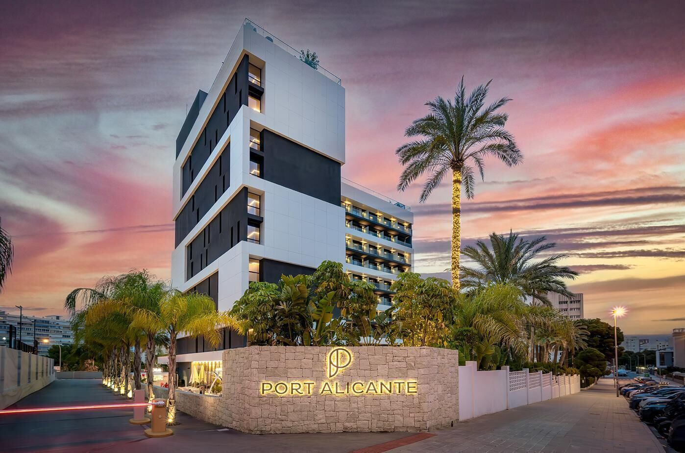 Um hotel moderno com uma placa de destaque com a inscrição "PORT ALICANTE" e uma palmeira em primeiro plano.