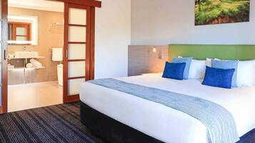 Quarto de hotel com uma cama grande, banheiro com espelho e um quadro na parede.