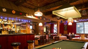 Uma área de bar com mesa de bilhar, banquetas de madeira e diversos acessórios.
