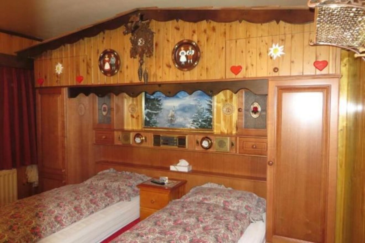 Quarto com painéis de madeira, duas camas, um quadro e um relógio na parede.