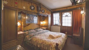 Um quarto aconchegante com cabeceira de madeira, colcha florida e uma janela grande com cortinas.