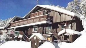 Uma cabana de madeira com varanda, rodeada por árvores cobertas de neve.