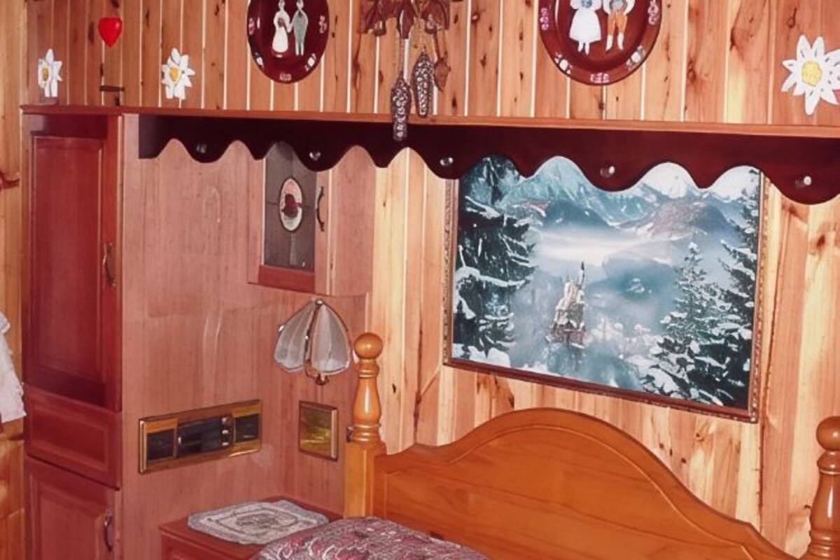 Um quarto de madeira com uma cama, um relógio e uma pintura de uma paisagem nevada.