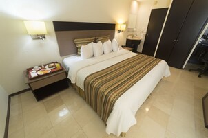 Quarto de hotel com cama, mesa de cabeceira com bandeja de café da manhã, mesa de apoio com abajur e guarda-roupa.