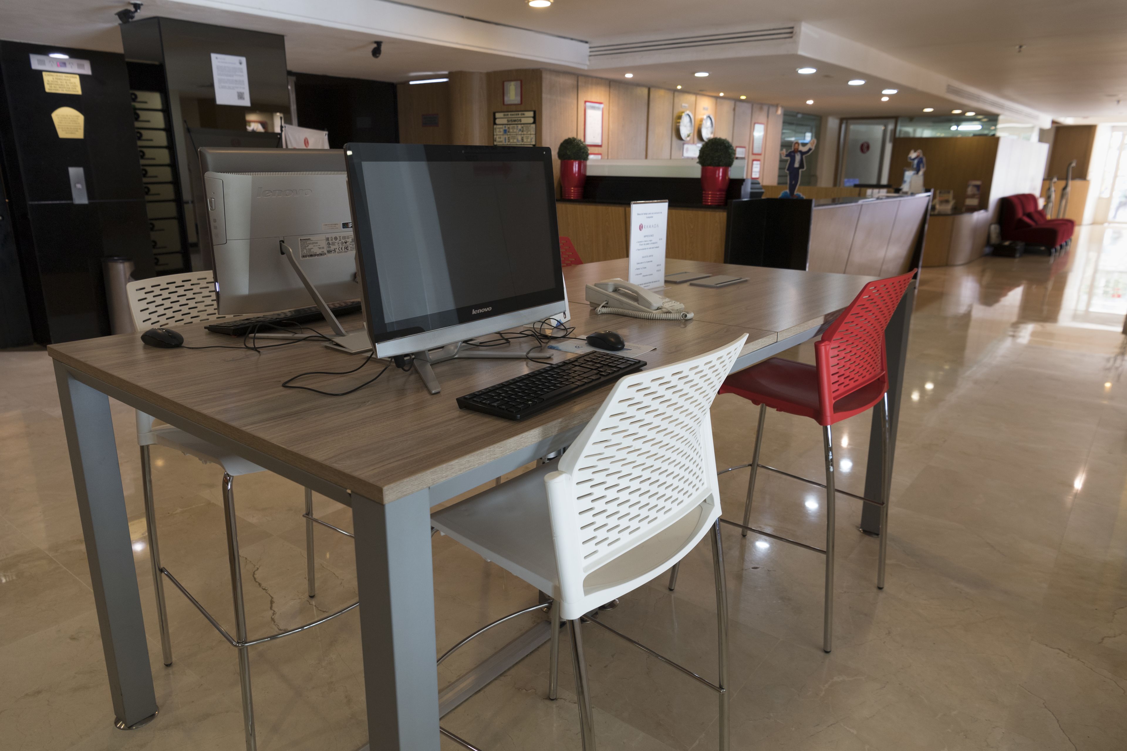 Bancada de recepção com computador, telefone e quadro de avisos. Cadeiras e um balcão ao fundo.