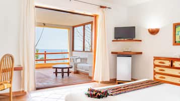 Quarto de hotel com cama, televisão, penteadeira, escrivaninha, cadeira e varanda com vista para o mar.