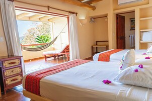 Quarto de hotel com duas camas, uma rede, uma cadeira de madeira e vista para o verde lá fora.