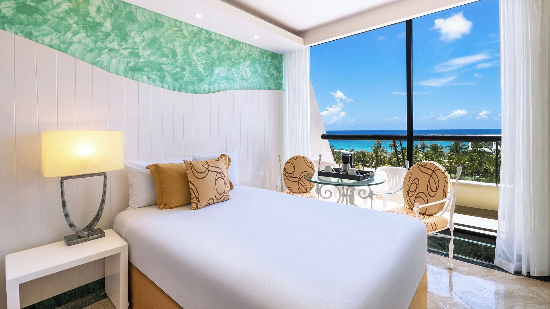 Quarto de hotel com uma cama, mesa de cabeceira, mesa com cadeiras e vista para o oceano.