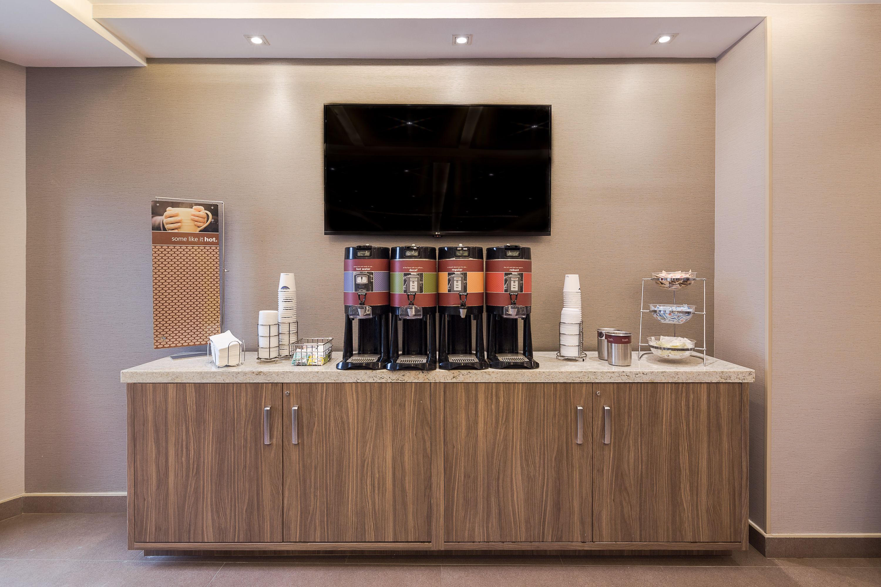Um espaço para café com vários dispensadores e uma televisão de tela plana na parede.