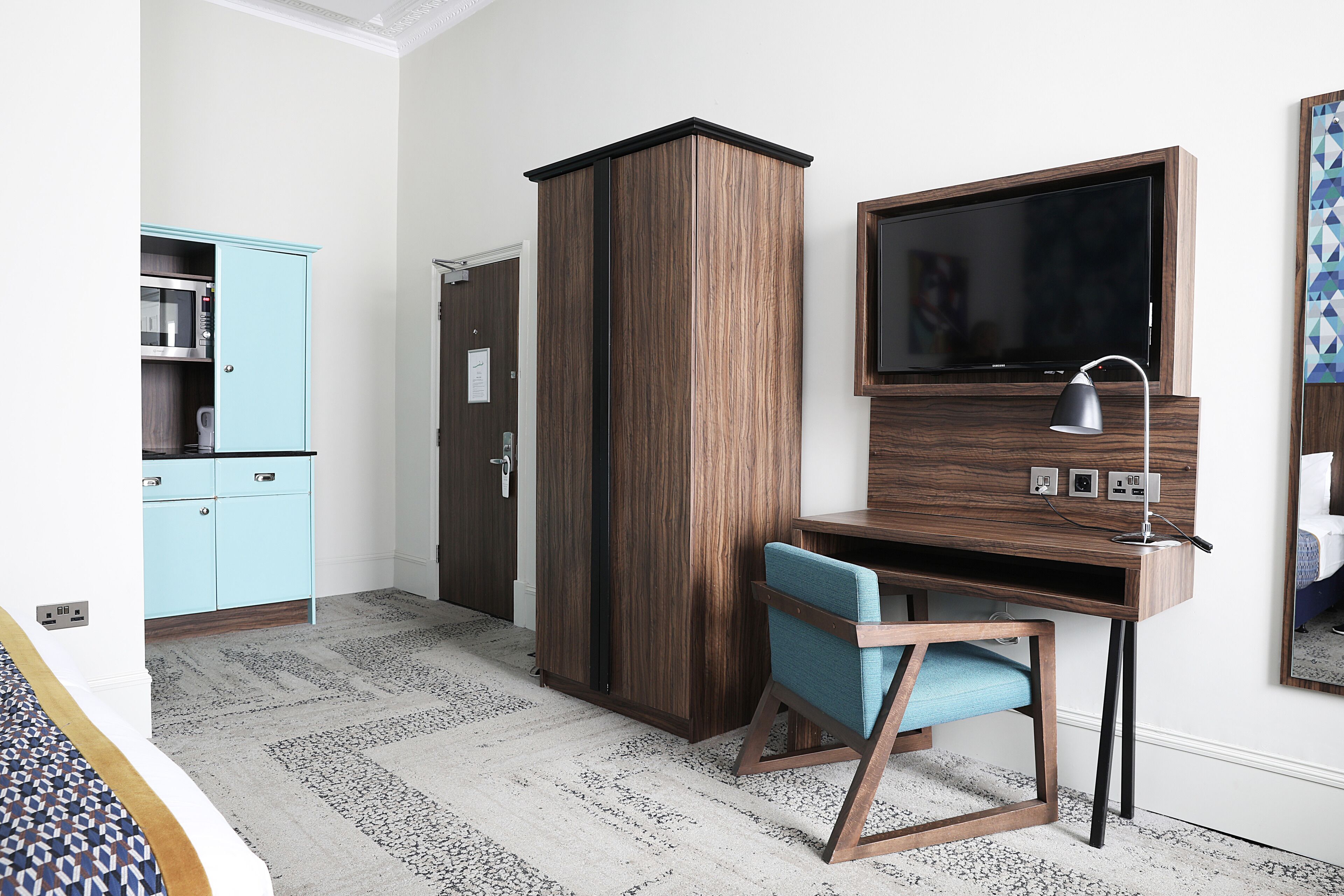 Quarto com escrivaninha, televisão, guarda-roupa e armário.