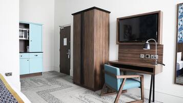Quarto com escrivaninha, televisão, guarda-roupa e armário.