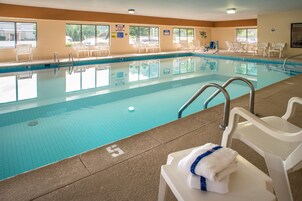 Piscina interna com água cristalina, cadeiras de lounge brancas e uma toalha em uma cadeira.