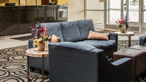 Um saguão com um sofá azul, uma mesa redonda pequena com um vaso e uma mesa de recepção.