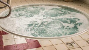 Uma banheira de hidromassagem com uma escada de metal, um vaso de planta e piso revestido de azulejos.