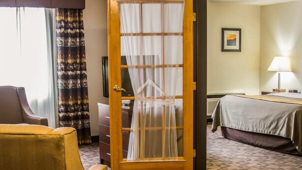 Quarto de hotel com cama, poltrona, escrivaninha e porta com cortina.