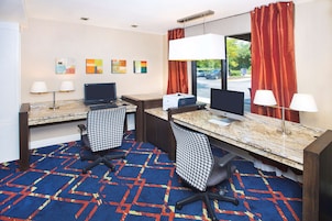 Quarto de hotel com duas mesas, duas cadeiras, piso coberto por carpete e obras de arte na parede.