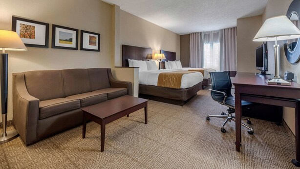 Quarto de hotel com cama, sofá, escrivaninha e televisão.