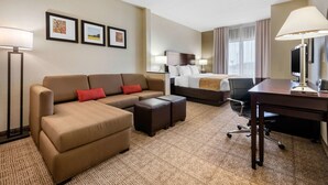 Quarto de hotel com sofá, cama, escrivaninha e televisão.