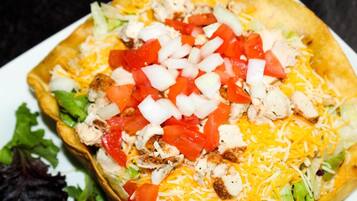 Uma tigela de tacos com queijo ralado, tomate picado e alface.