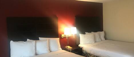 Quarto de hotel com duas camas, uma mesa de cabeceira com abajur e parede estampada.