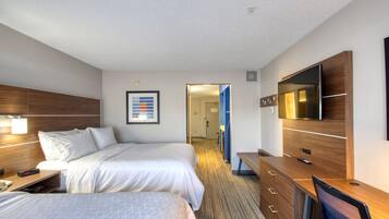 Quarto de hotel com duas camas, uma escrivaninha, televisão e banheiro visível através de uma porta aberta.