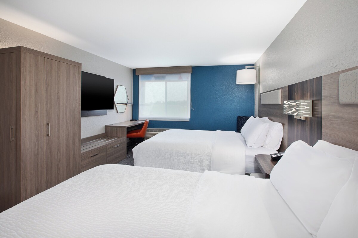 Quarto de hotel com duas camas, uma escrivaninha, uma cadeira, uma TV e uma janela com vista.