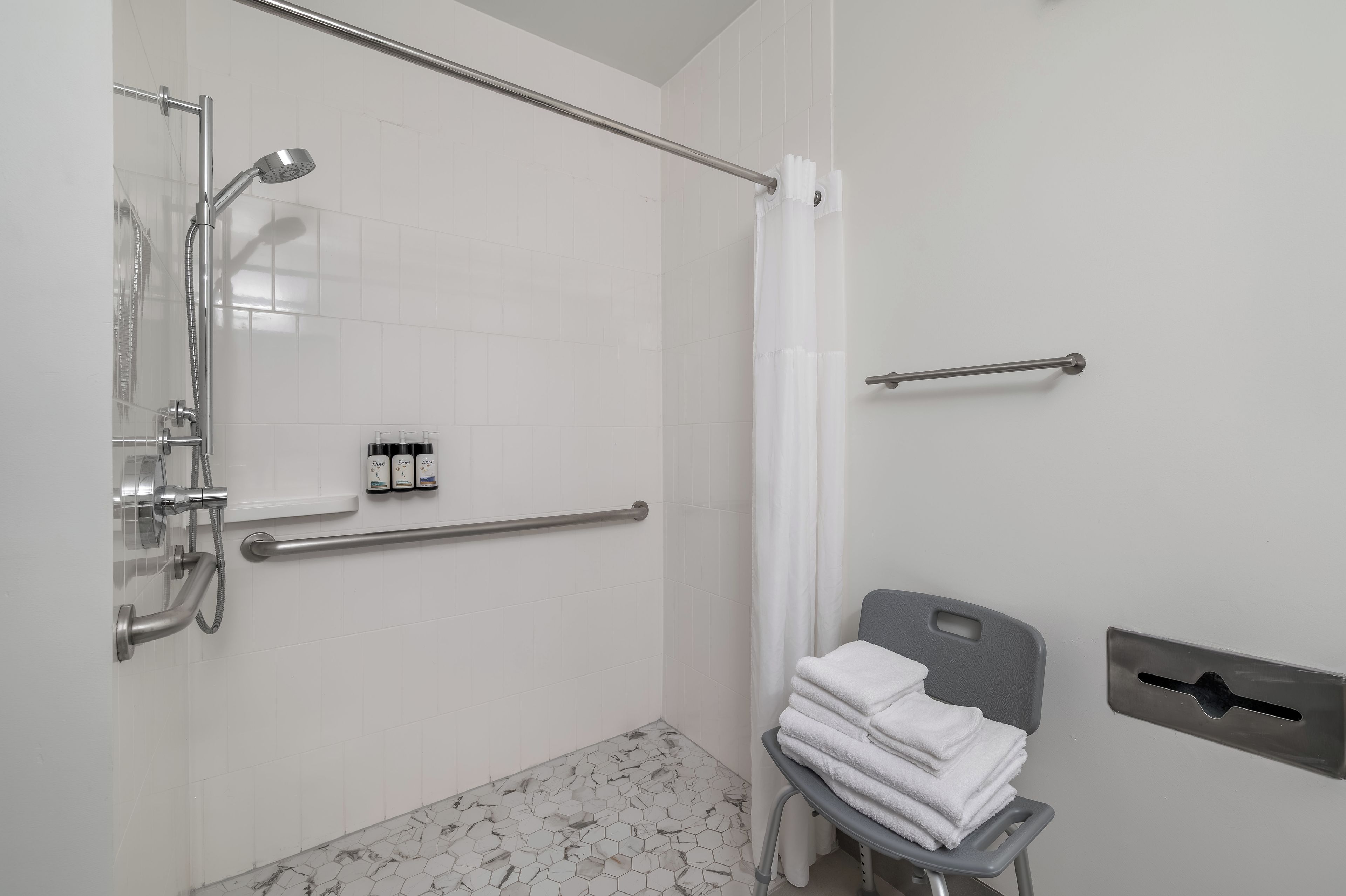 Área de duche com barra de apoio, suporte para toalhas e chuveiro.