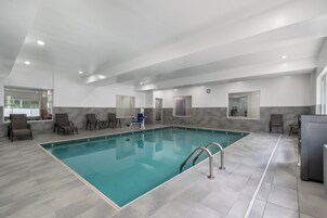 Uma grande piscina coberta com piso de azulejos, rodeada por espreguiçadeiras e um vestiário.