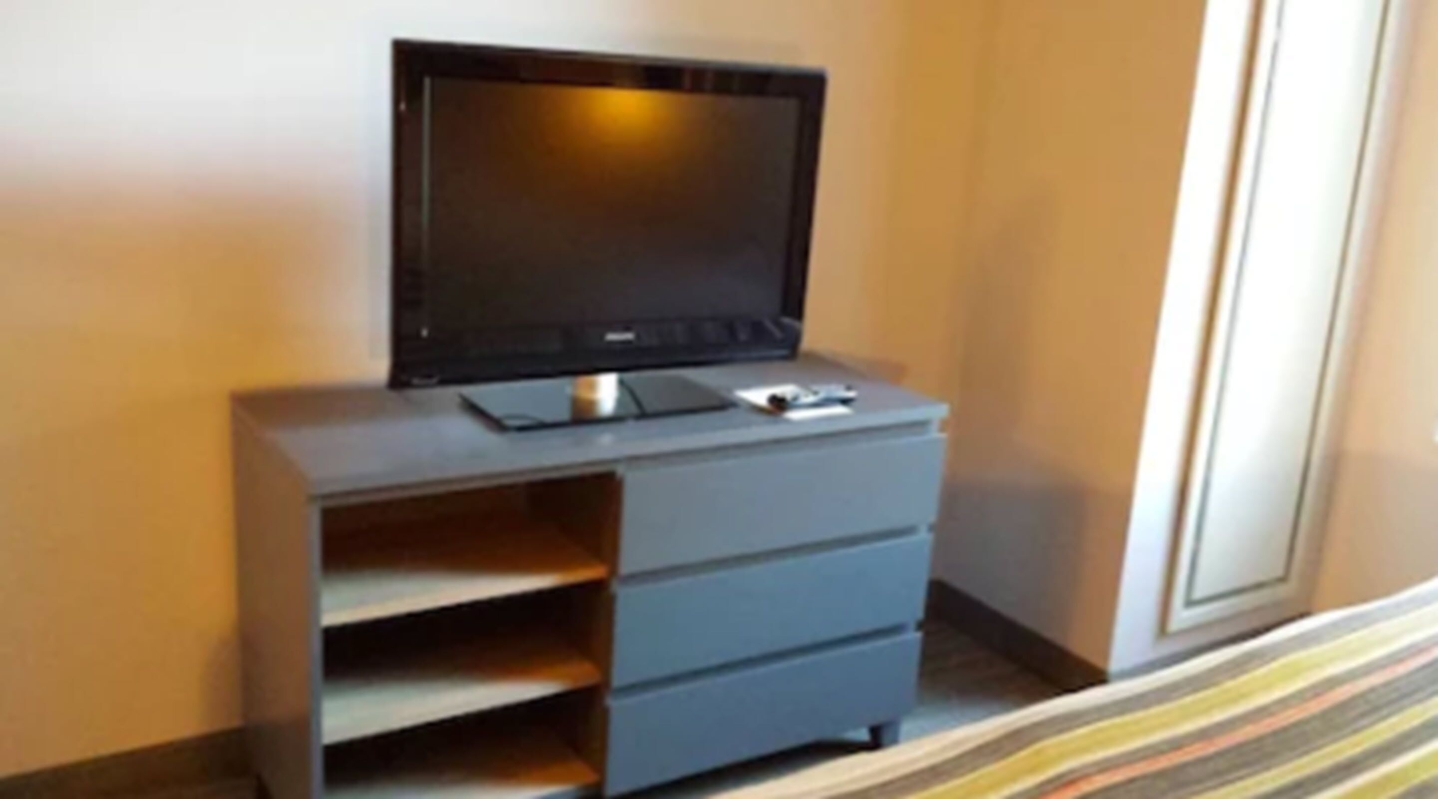 Uma pequena mesa escura com uma TV de tela plana, um laptop e um controle remoto.
