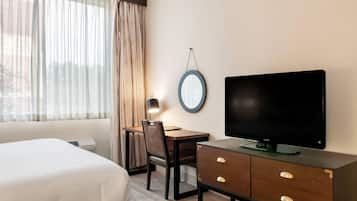 Quarto de hotel com uma cama, uma escrivaninha com cadeira, televisão num móvel e uma janela com cortinas.