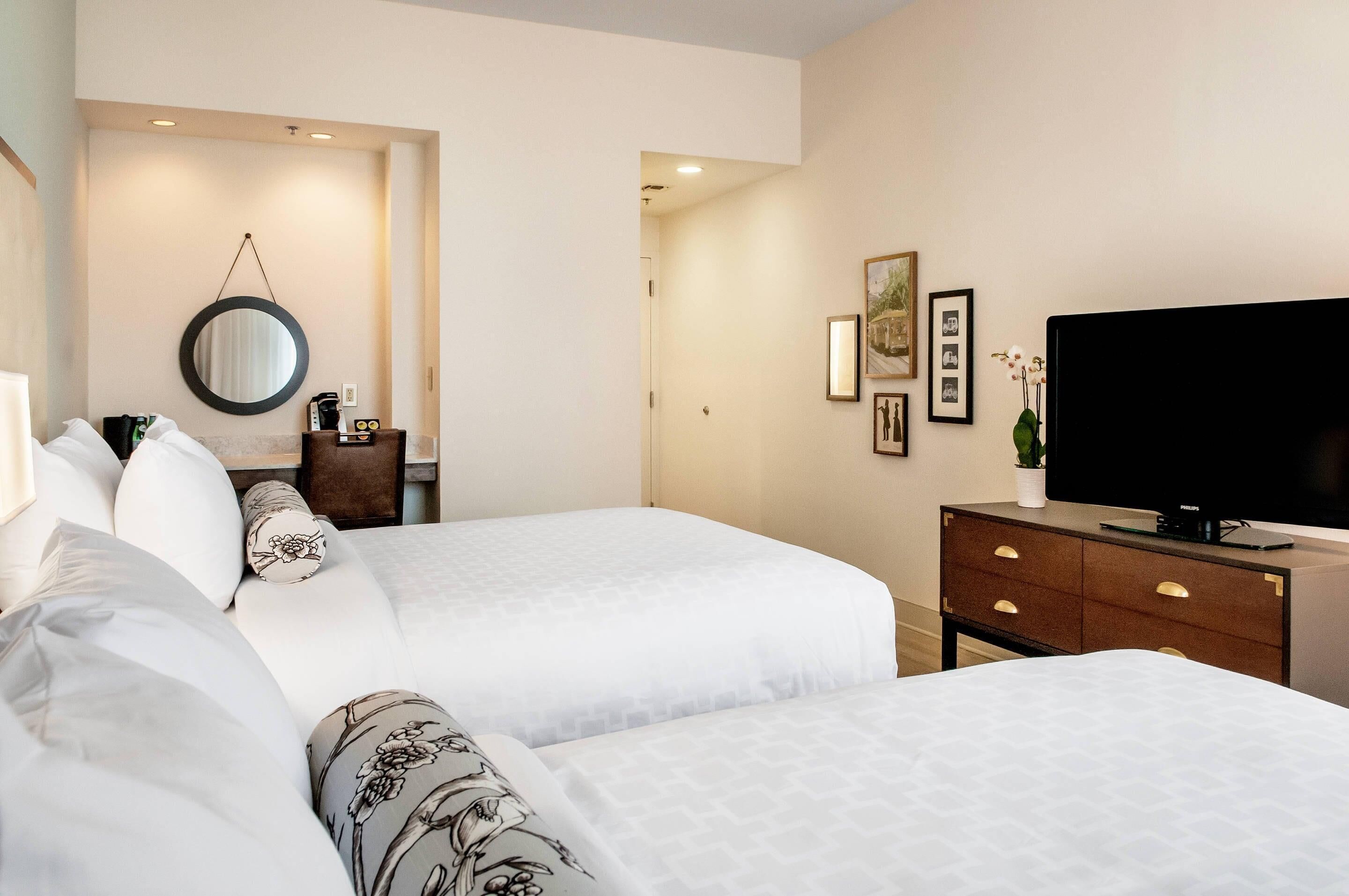 Quarto de hotel com duas camas, televisão, penteadeira e espelho.