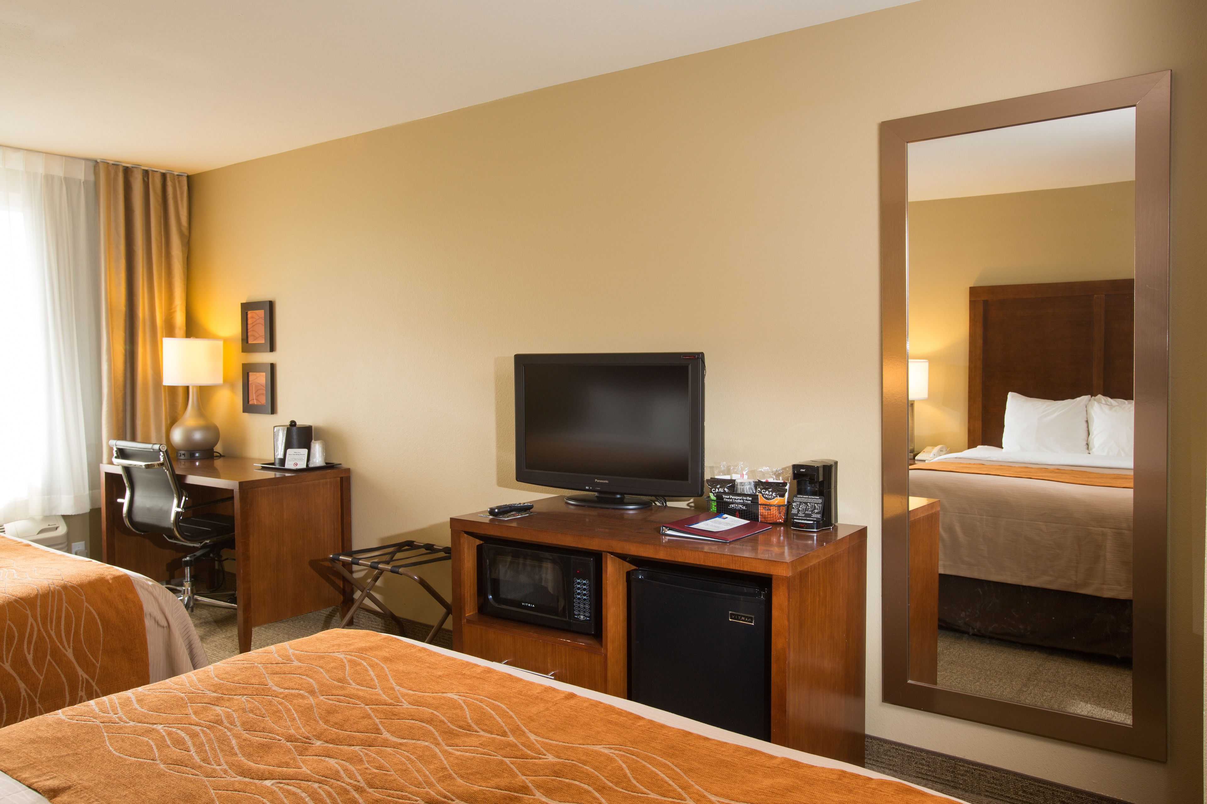 Quarto de hotel com duas camas, uma escrivaninha com computador, televisão, micro-ondas e frigorífico.