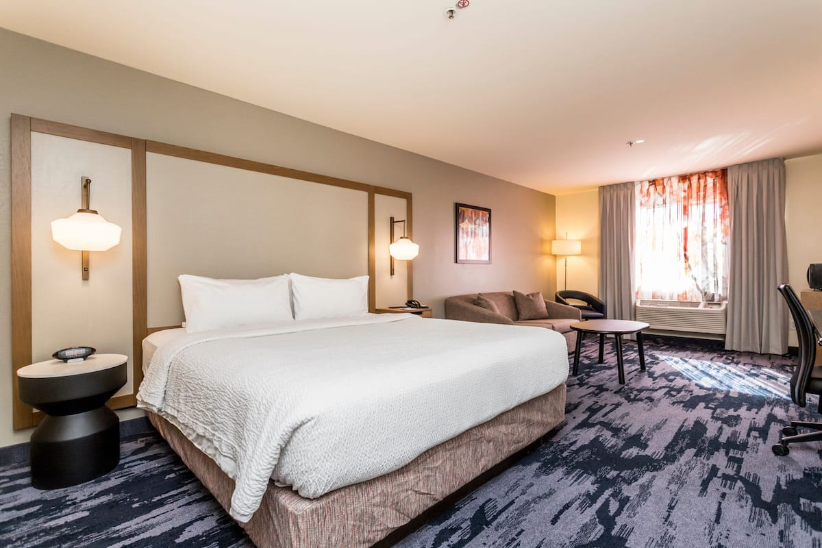 Quarto de hotel com uma cama grande, duas mesas de cabeceira, uma escrivaninha, uma cadeira e uma janela com cortinas.