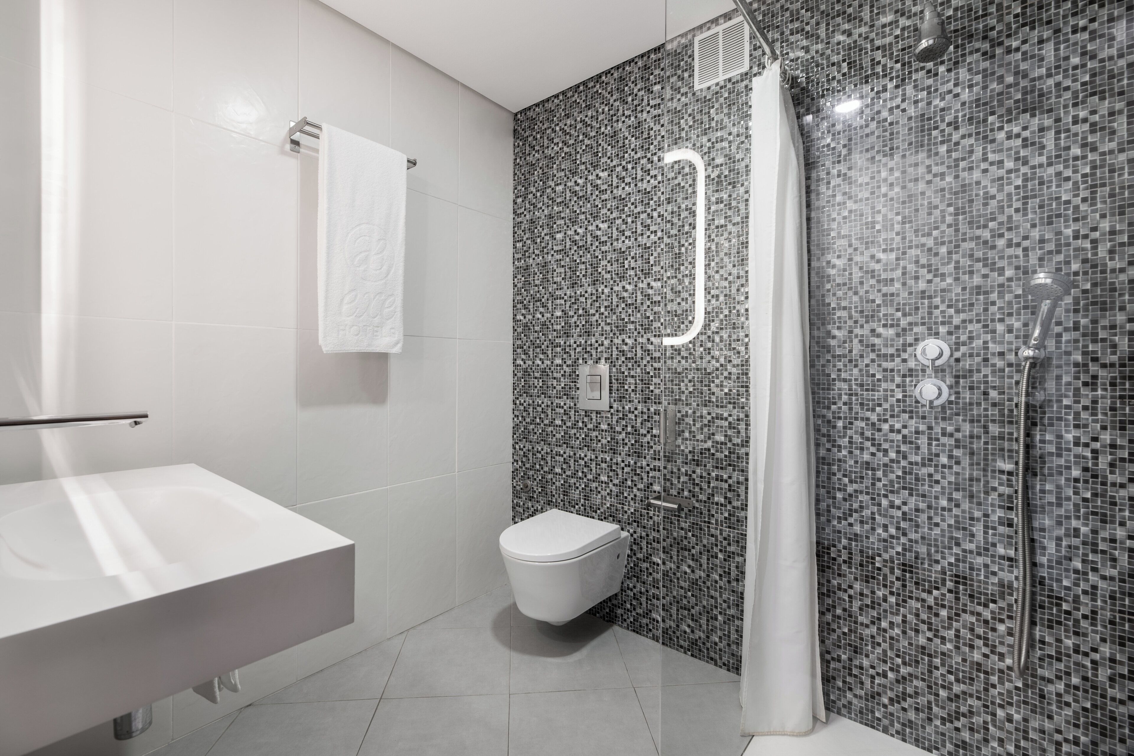 Um banheiro moderno com pia branca, vaso sanitário e chuveiro com parede de mosaico.
