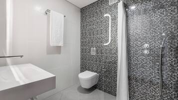 Um banheiro moderno com pia branca, vaso sanitário e chuveiro com parede de mosaico.