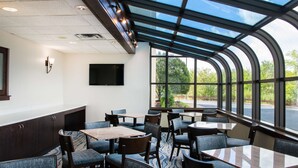 Um restaurante com teto de vidro curvo, mesas, cadeiras e uma televisão de tela plana na parede.