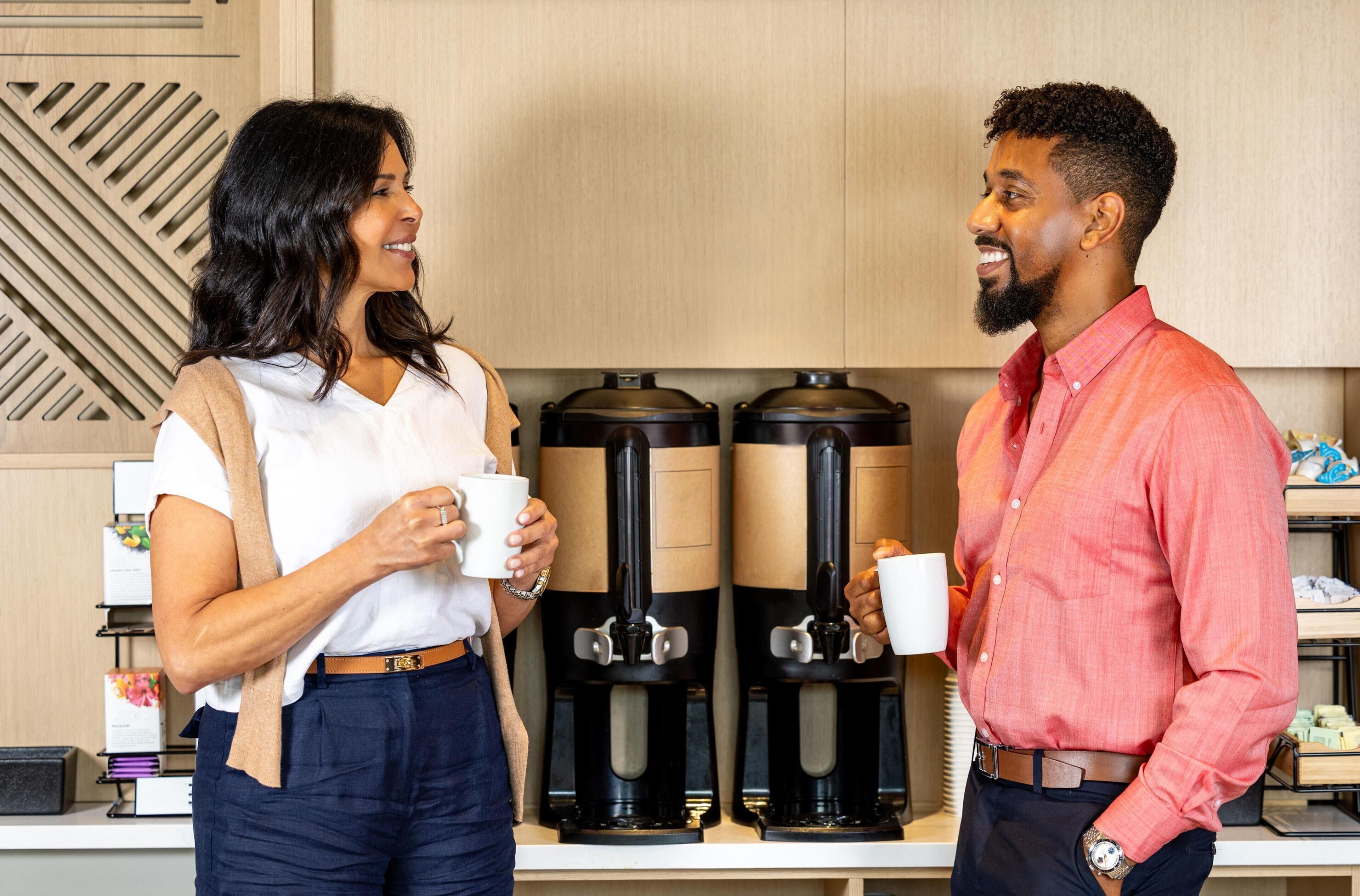 Duas pessoas em um café, com máquinas de café e um balcão.