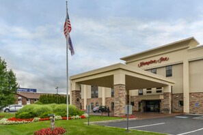 Um Hampton Inn com entrada coberta, pilares de pedra e estacionamento.